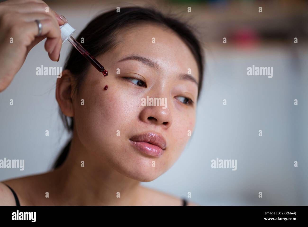 Crop young ethnic female covering cheeks with cream blush with pipette ...