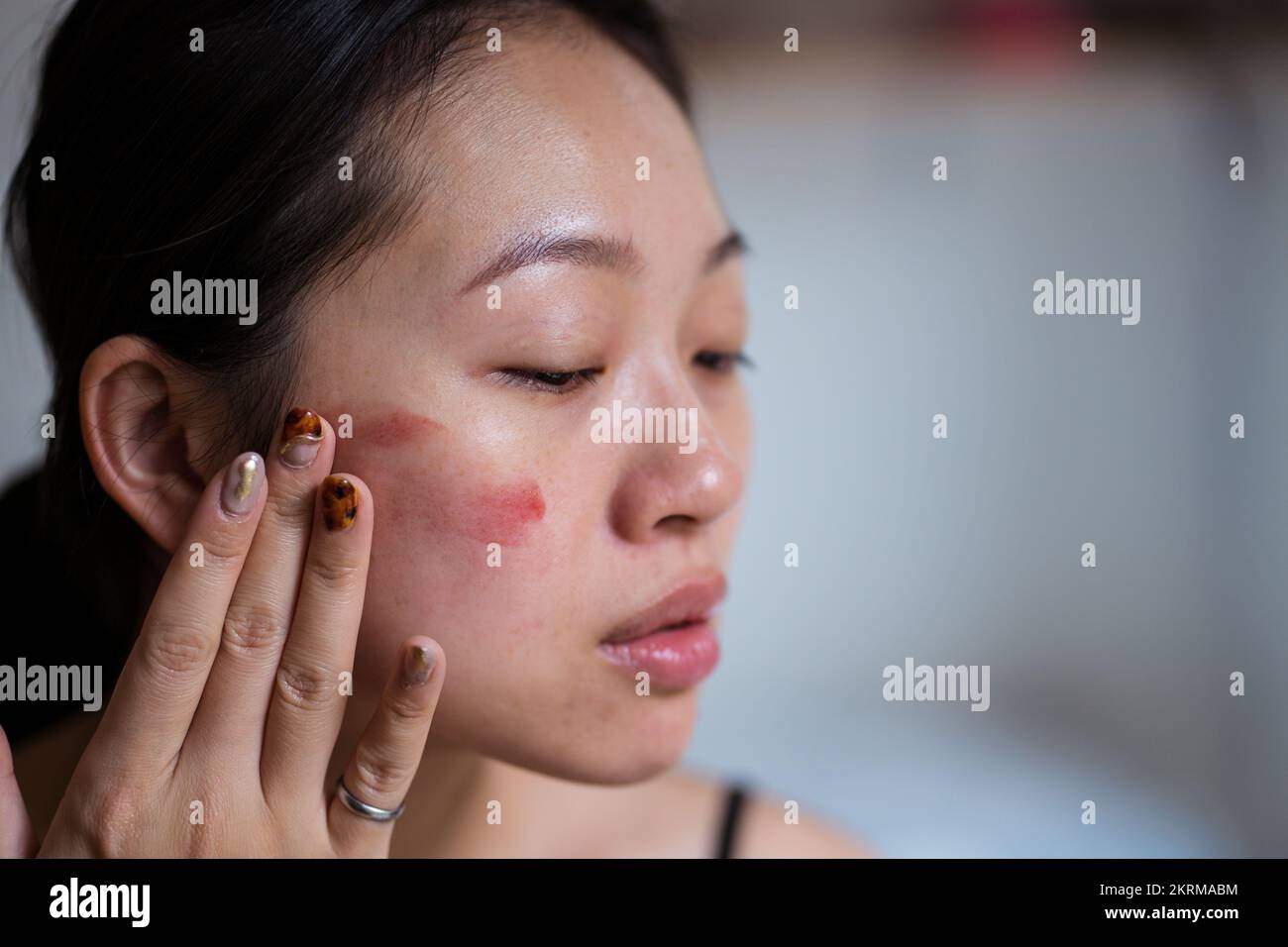 Crop young ethnic female covering cheeks with cream blush while putting ...
