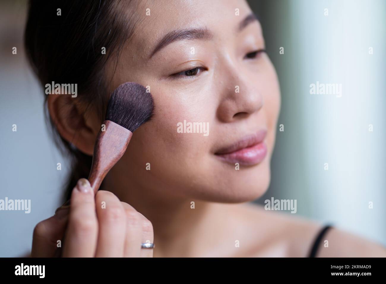 Crop ethnic female spreading powder and blush on cheeks while looking ...