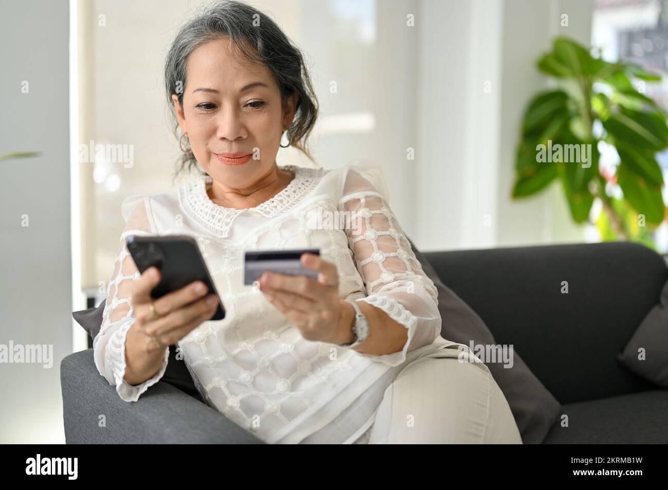 Happy and relaxed Asian aged retire woman sitting on sofa in her living ...