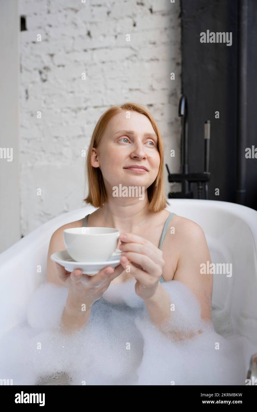 Young positive female with bob haircut in bra relaxing in bathtub with ...