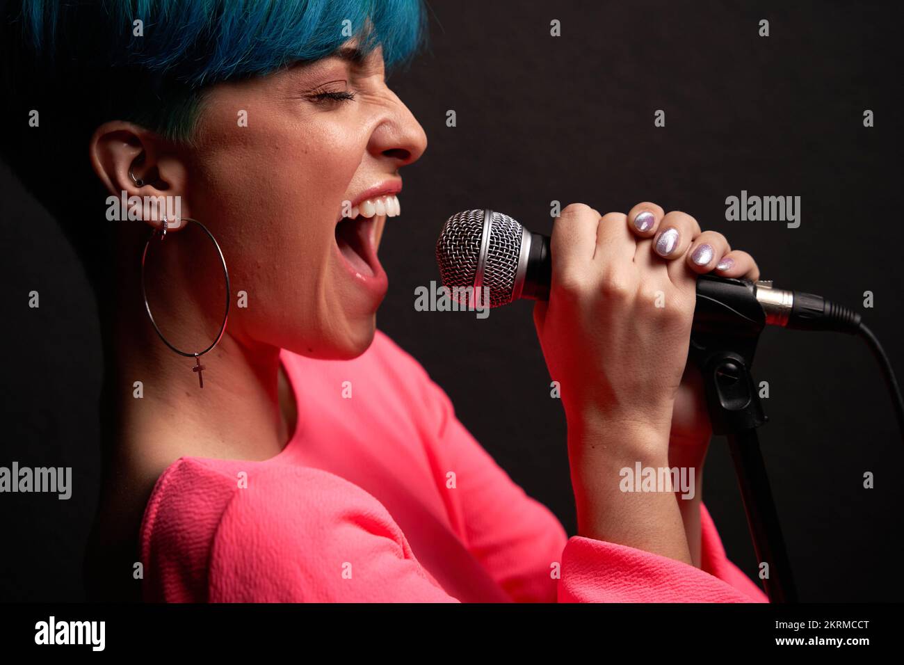 Side view of young female in casual clothes holding microphone while ...