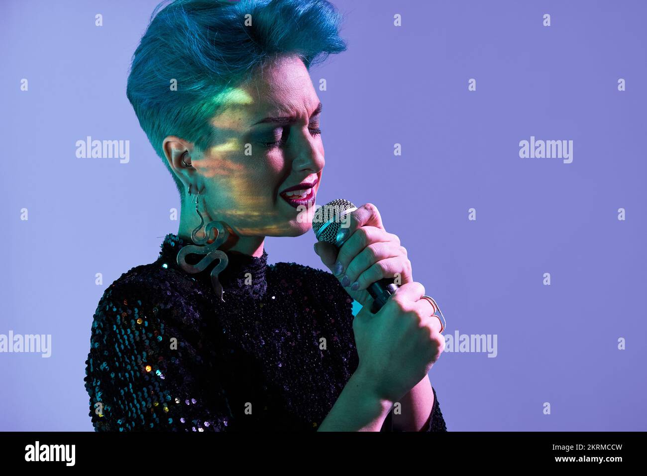 Positive young female singer in casual clothes with microphone in light ...
