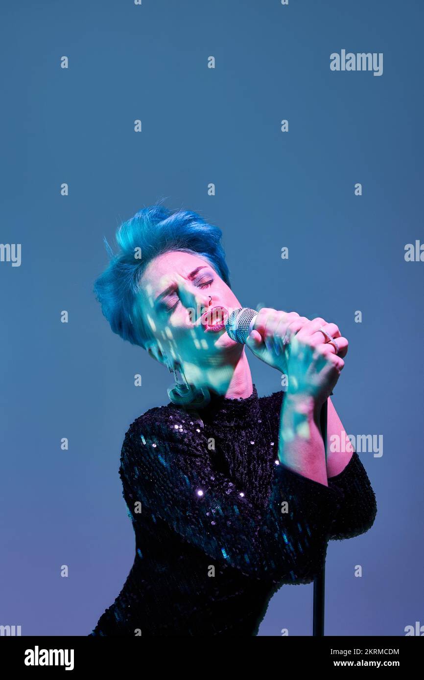 Positive young female singer in casual clothes with microphone in light ...