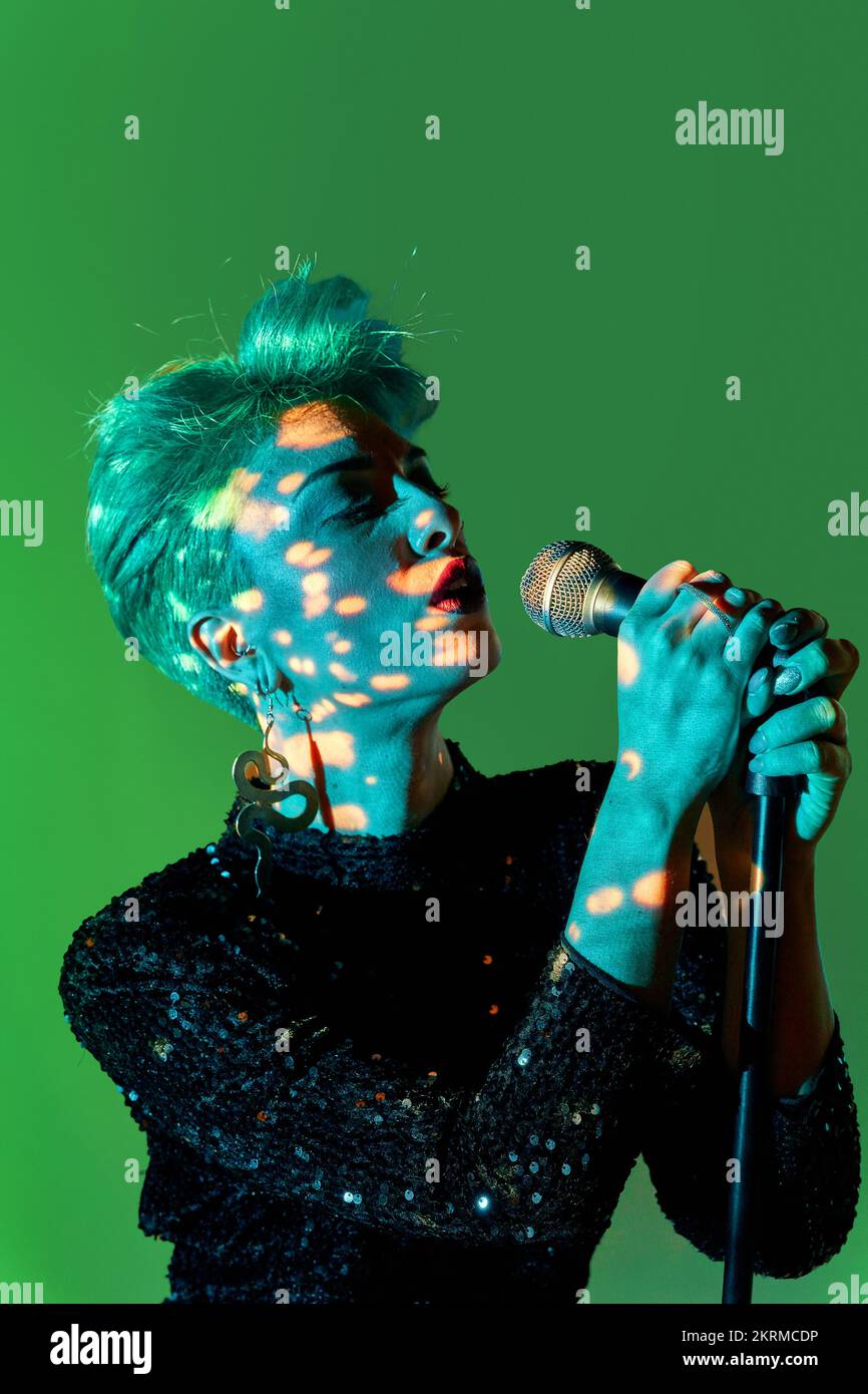 Positive young female singer in casual clothes with microphone in light ...