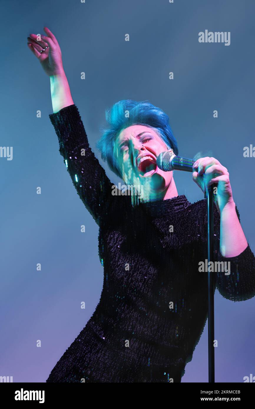 Positive young female singer in casual clothes with microphone in light ...