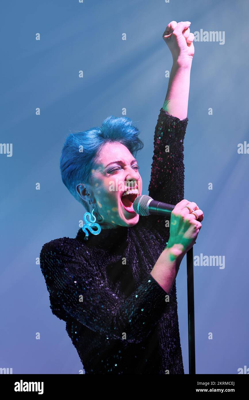 Positive young female singer in casual clothes with microphone in light ...