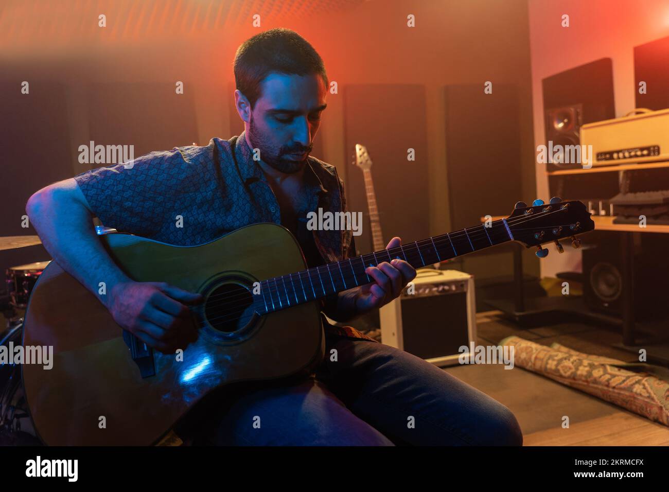 Concentrated male guitarist sitting in modern studio with glowing red ...