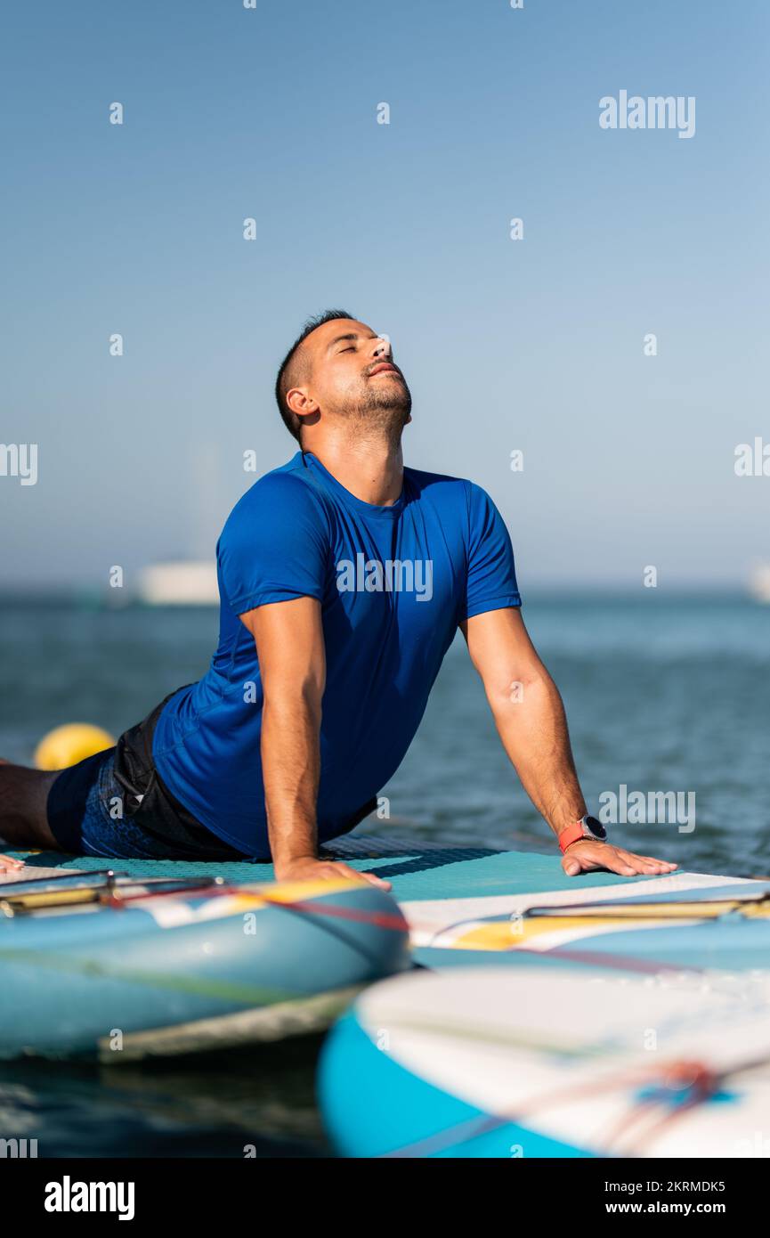 Calm adult male doing Upward Facing dog yoga pose on paddleboard while ...
