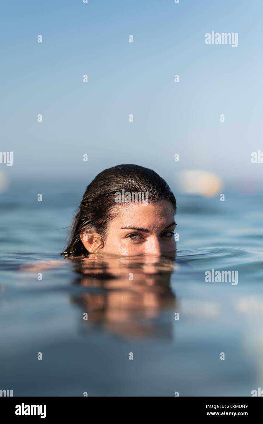 Female with dark wet hair swimming in calm water of sea while looking ...