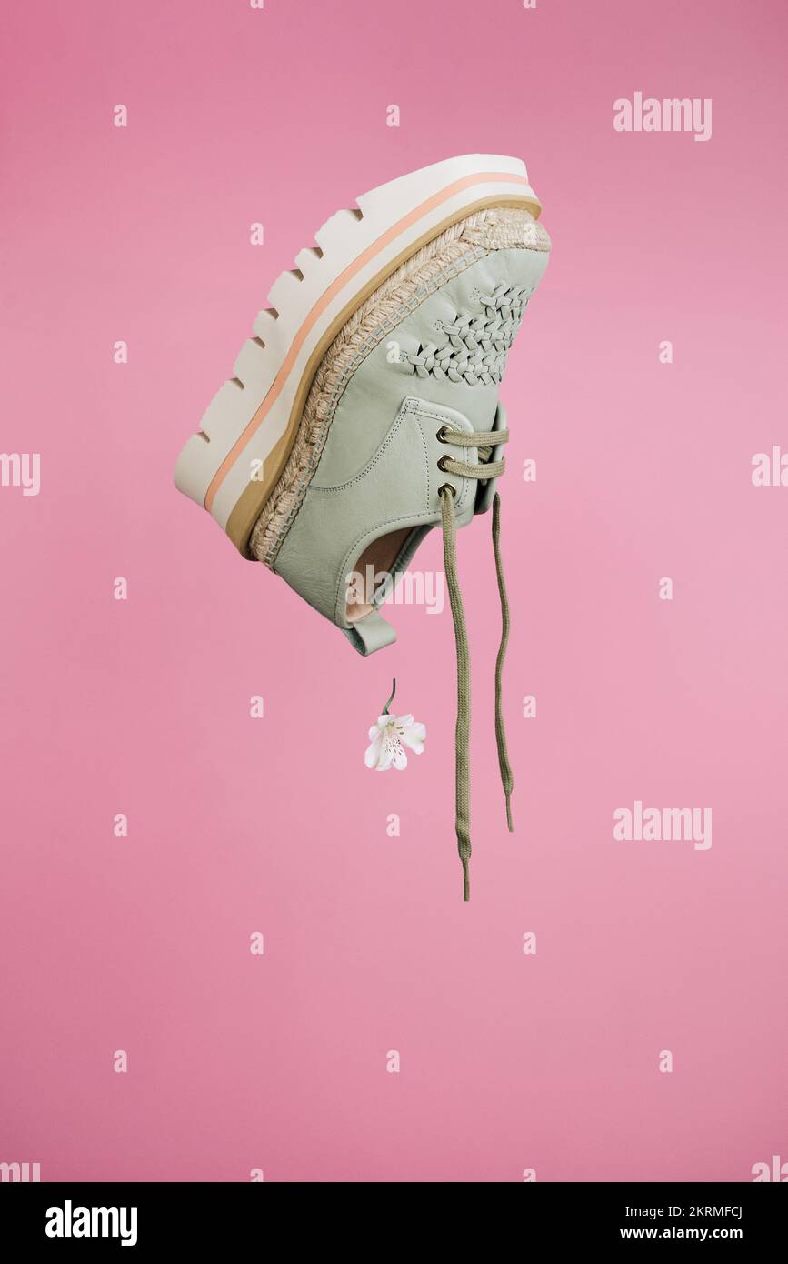 Tiny white flower falling from stylish shoe levitating against pink ...