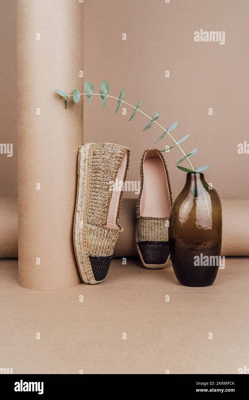 Stylish wicker slippers placed on beige background near vase with ...