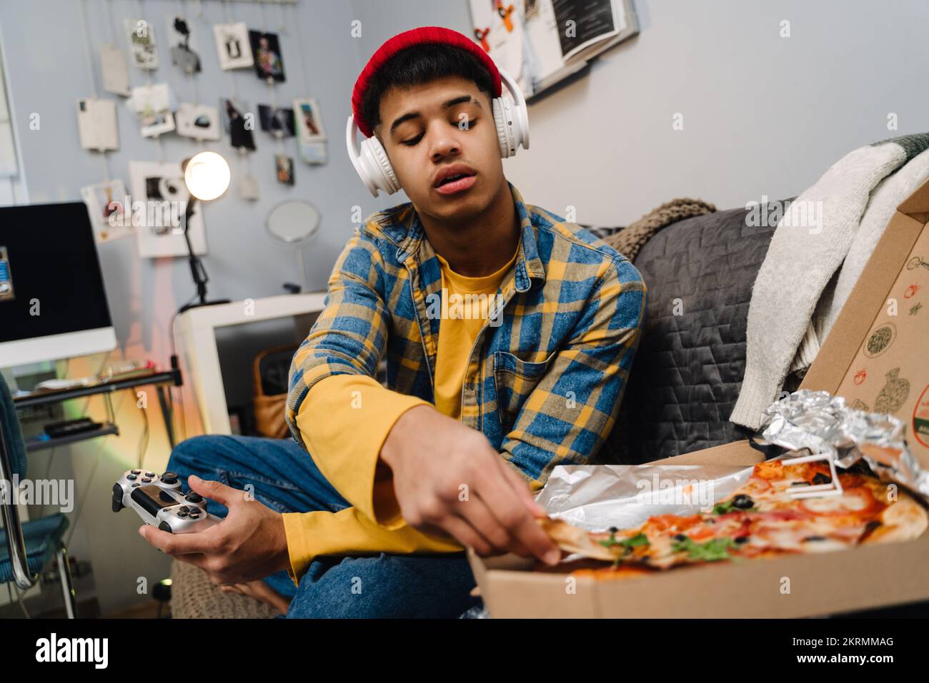 Middle-eastern teenage boy eating pizza and using controller while ...