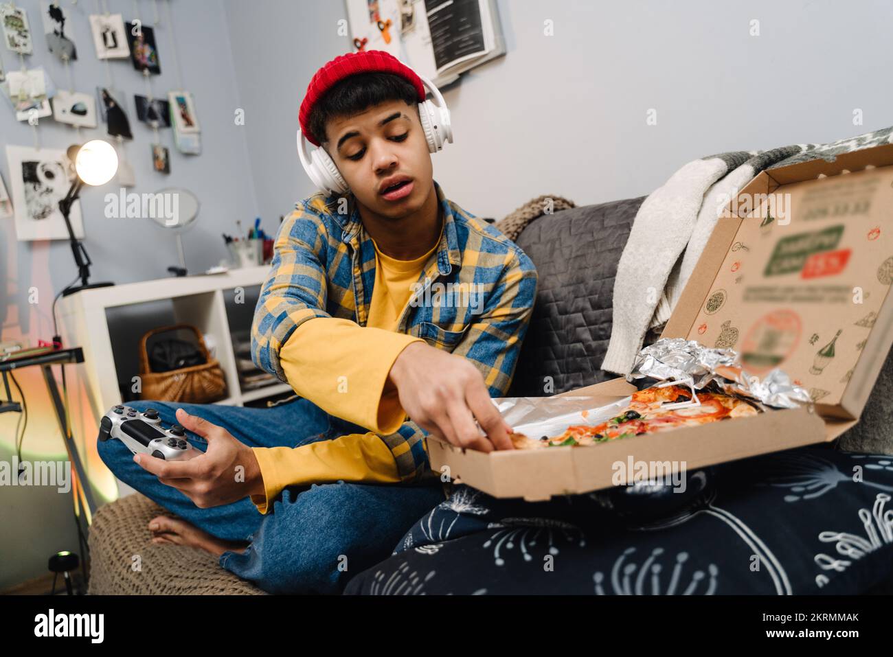 Middle-eastern teenage boy eating pizza and using controller while ...