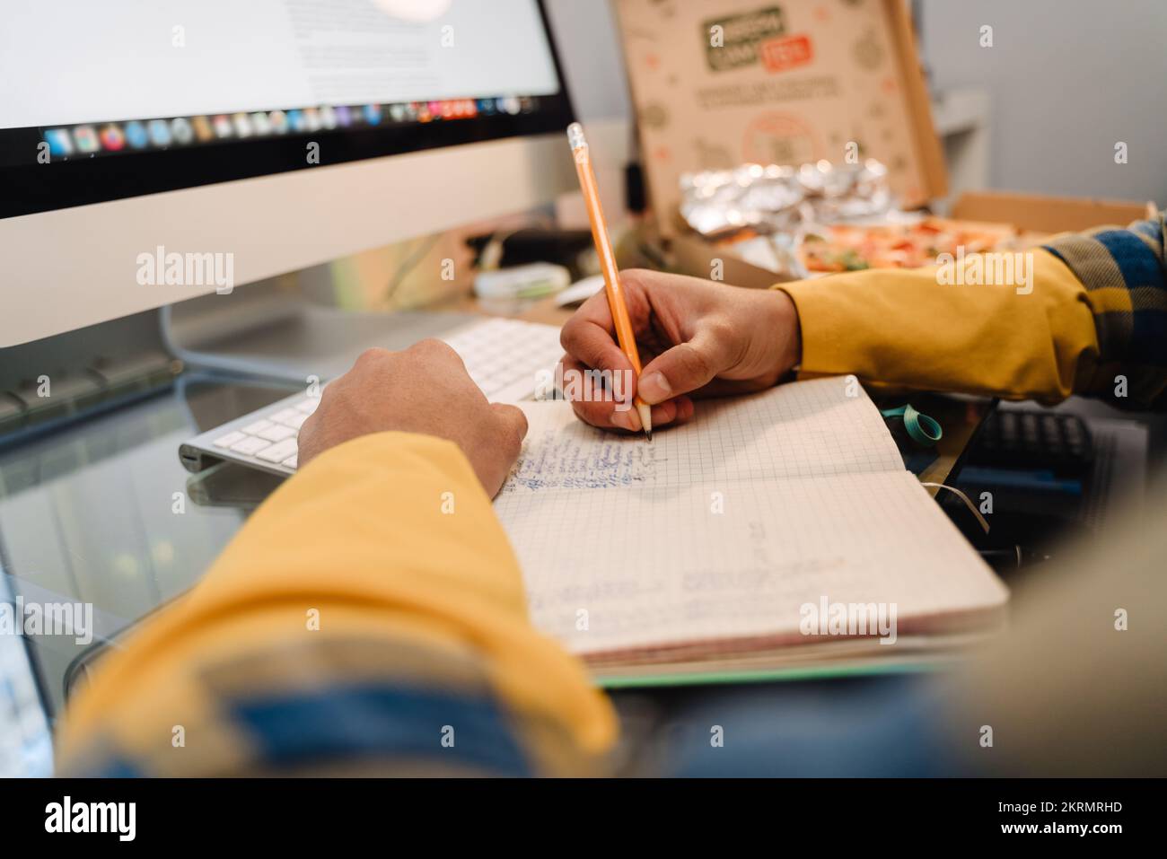 Teenage boy writing in exercise book and using desktop computer while ...