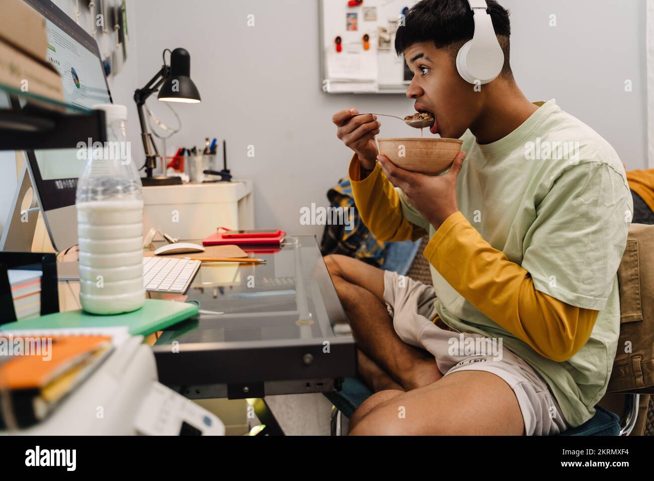 Brunette teenage boy using desktop computer while eating breakfast in ...