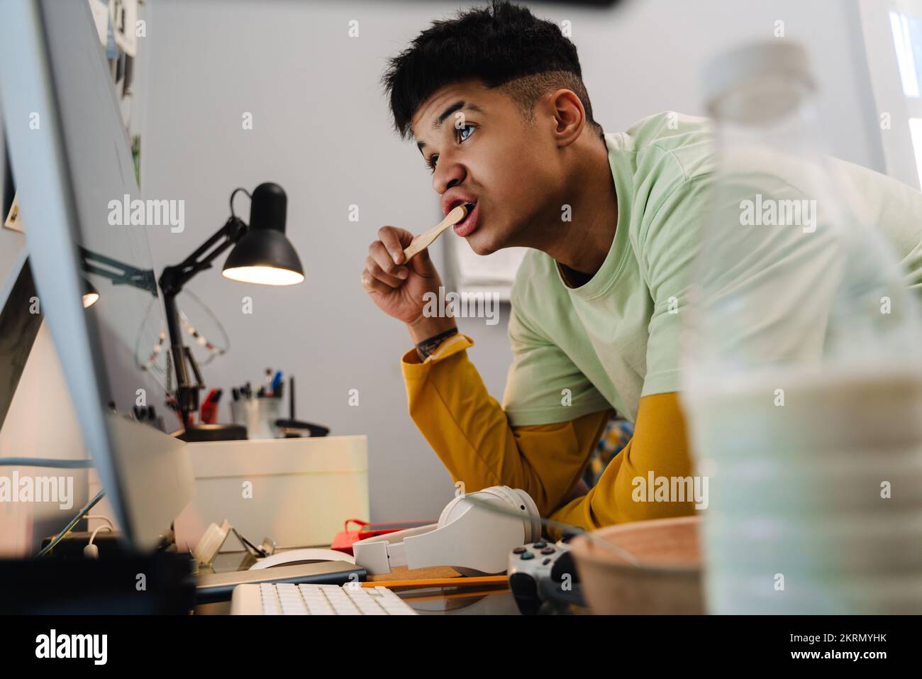 Brunette teenage boy brushing his teeth and looking at desktop computer ...