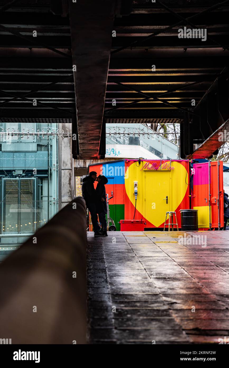 A young couple in a romantic embrace beneath Waterloo Bridge in London ...