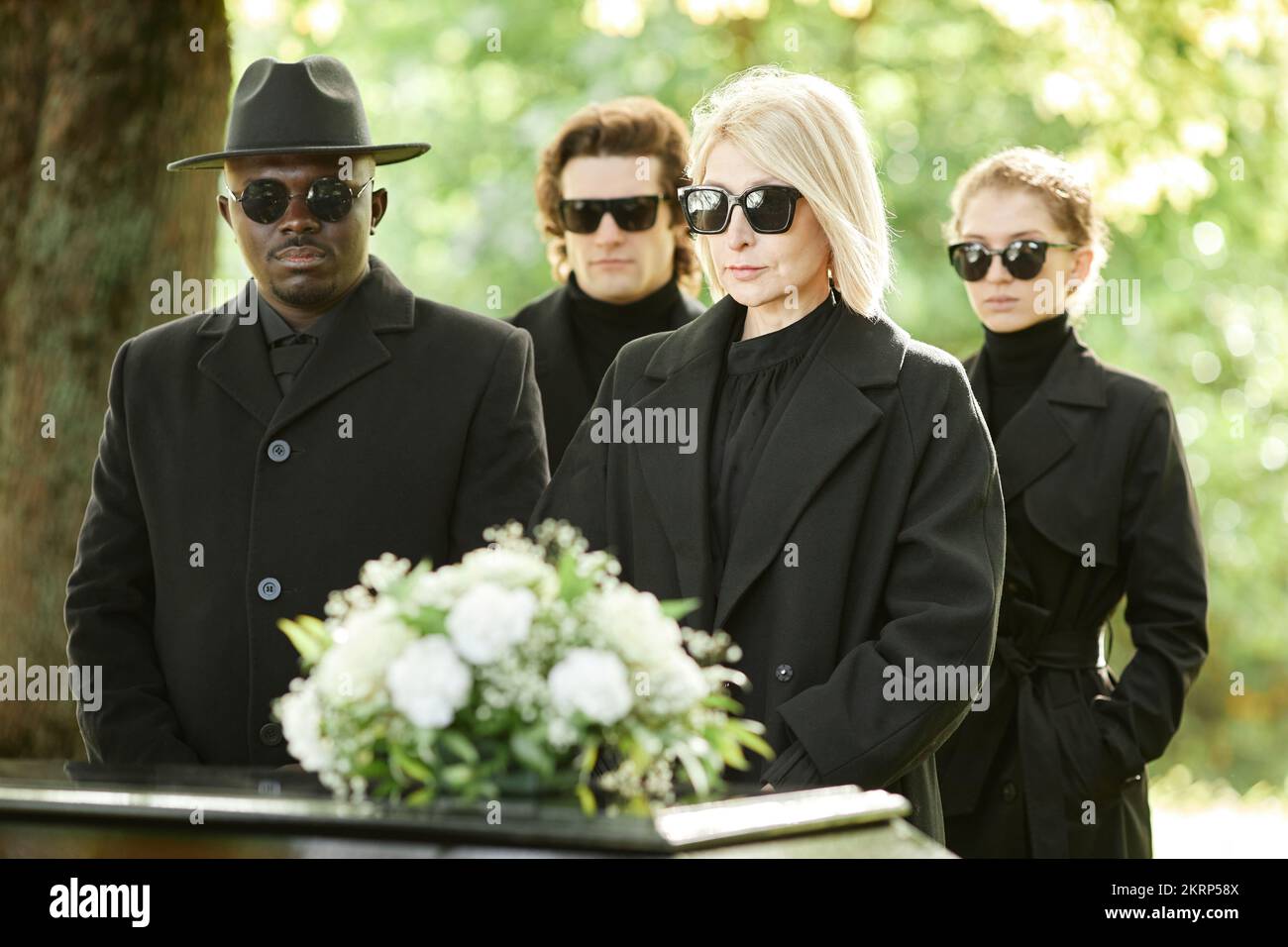Group of people wearing all black standing by coffin at outdoor funeral ...