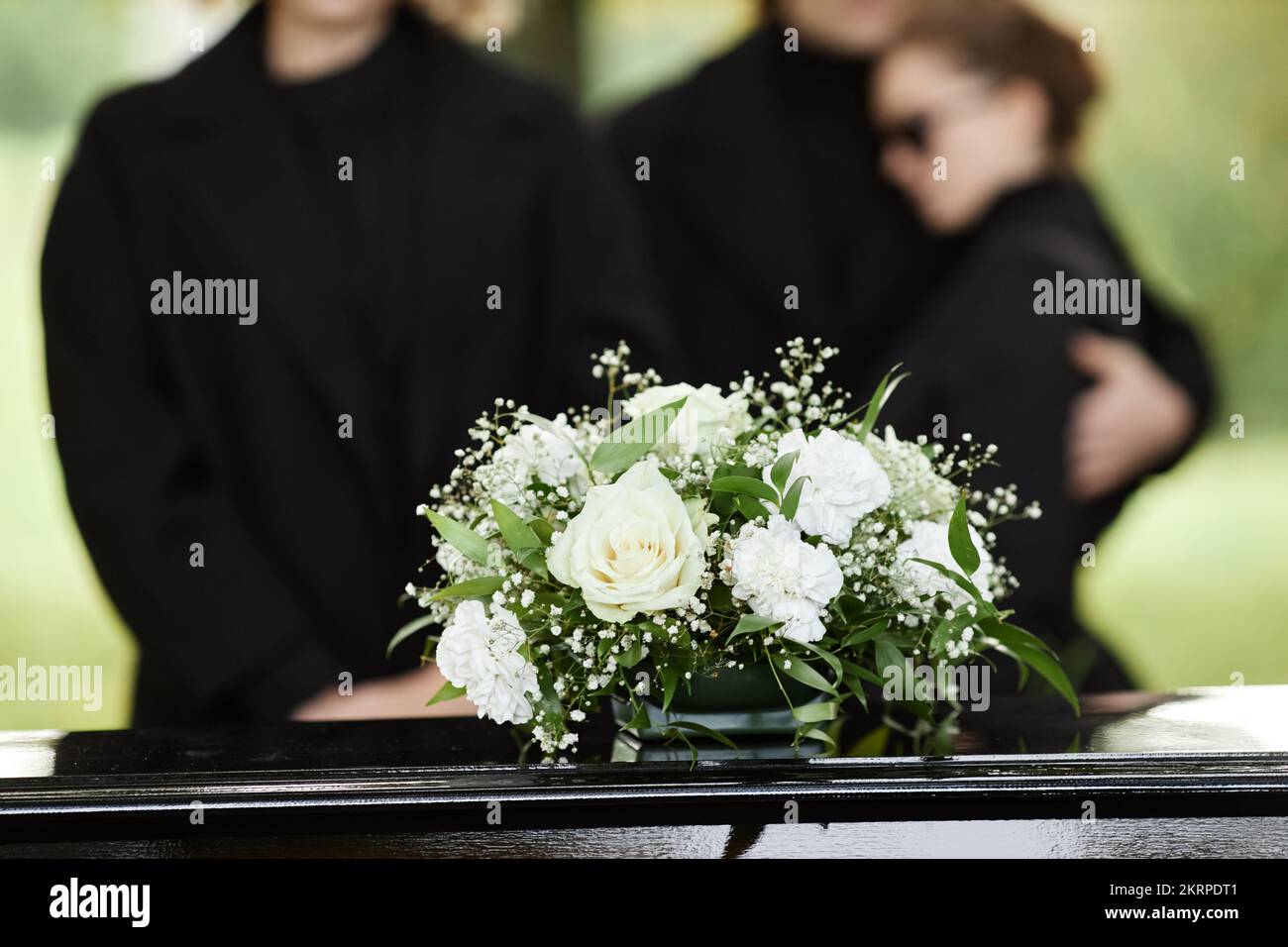 Close up of flower bouquet on coffin with people wearing black in ...