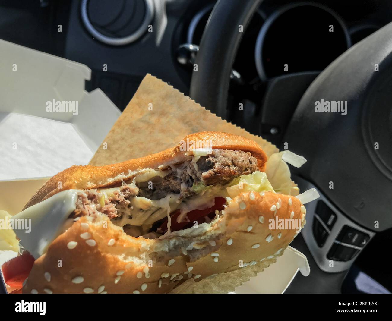 Eating while driving: a bitten burger in the hands inside the car ...