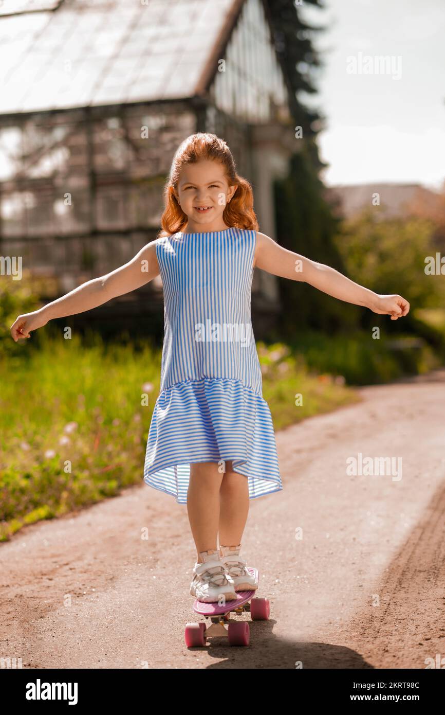 Ginger girl in a blue dress on a skateboard Stock Photo - Alamy