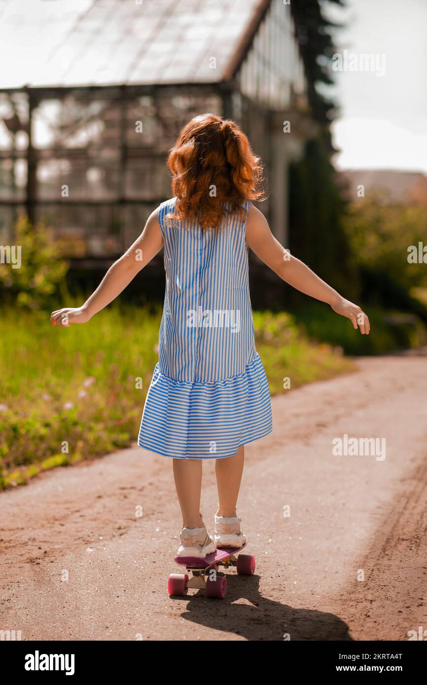 Ginger girl in a blue dress on a skateboard Stock Photo - Alamy