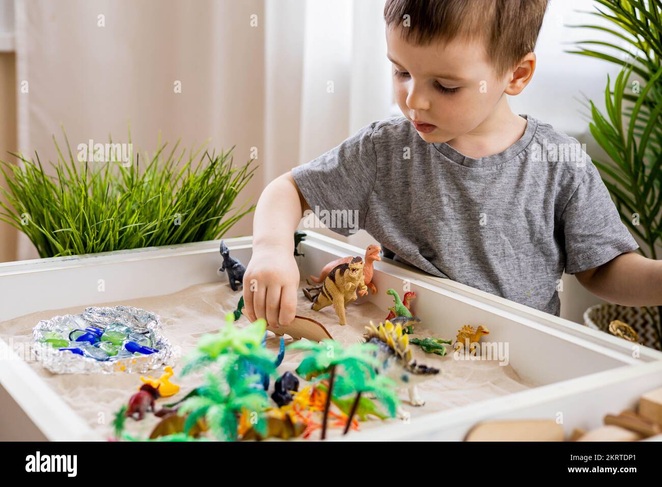 Cute baby boy playing sensory box kinetic sand table with carnivorous ...