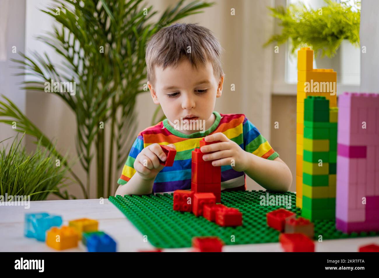 Confident male baby constructing tower with multicolored plastic pieces ...