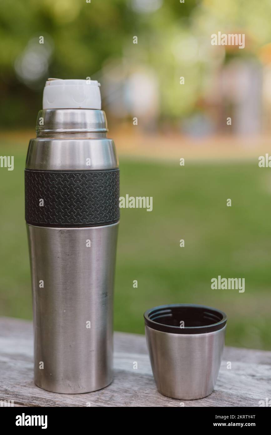 Stainless steel cup, mug with thermos stands on a wooden table in the ...