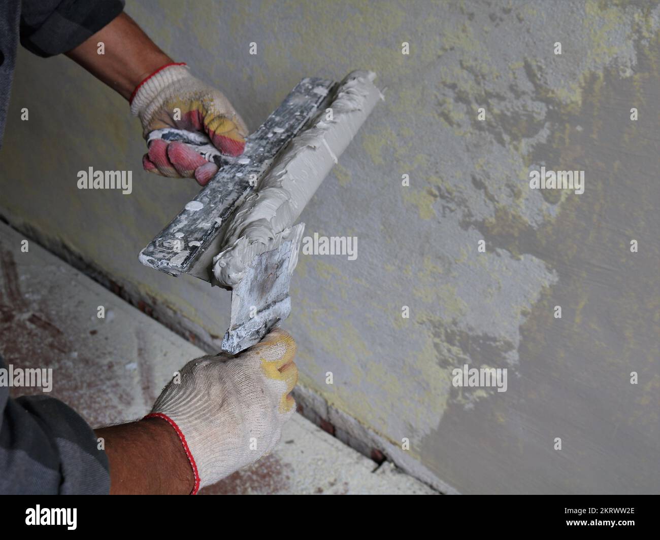 hands of a plasterer in fabric gloves with two spatulas while working ...