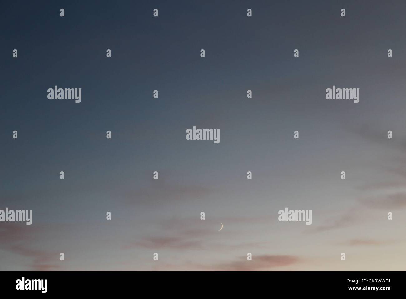 Faint moon in a twilight sky with dark blue to light yellowish gradient ...