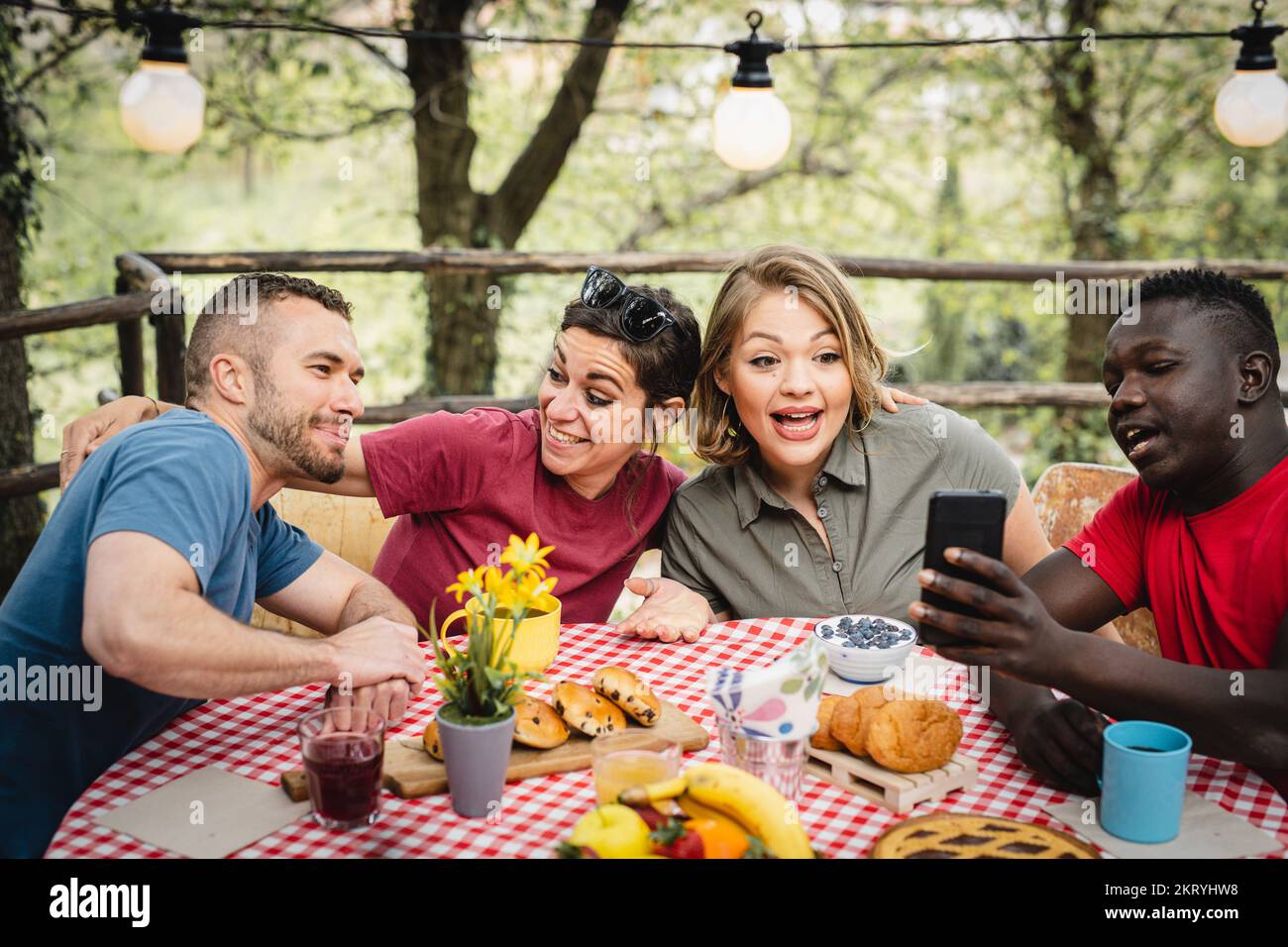 happy friends having breakfast in the backyard, young influencer using smartphone to create ...