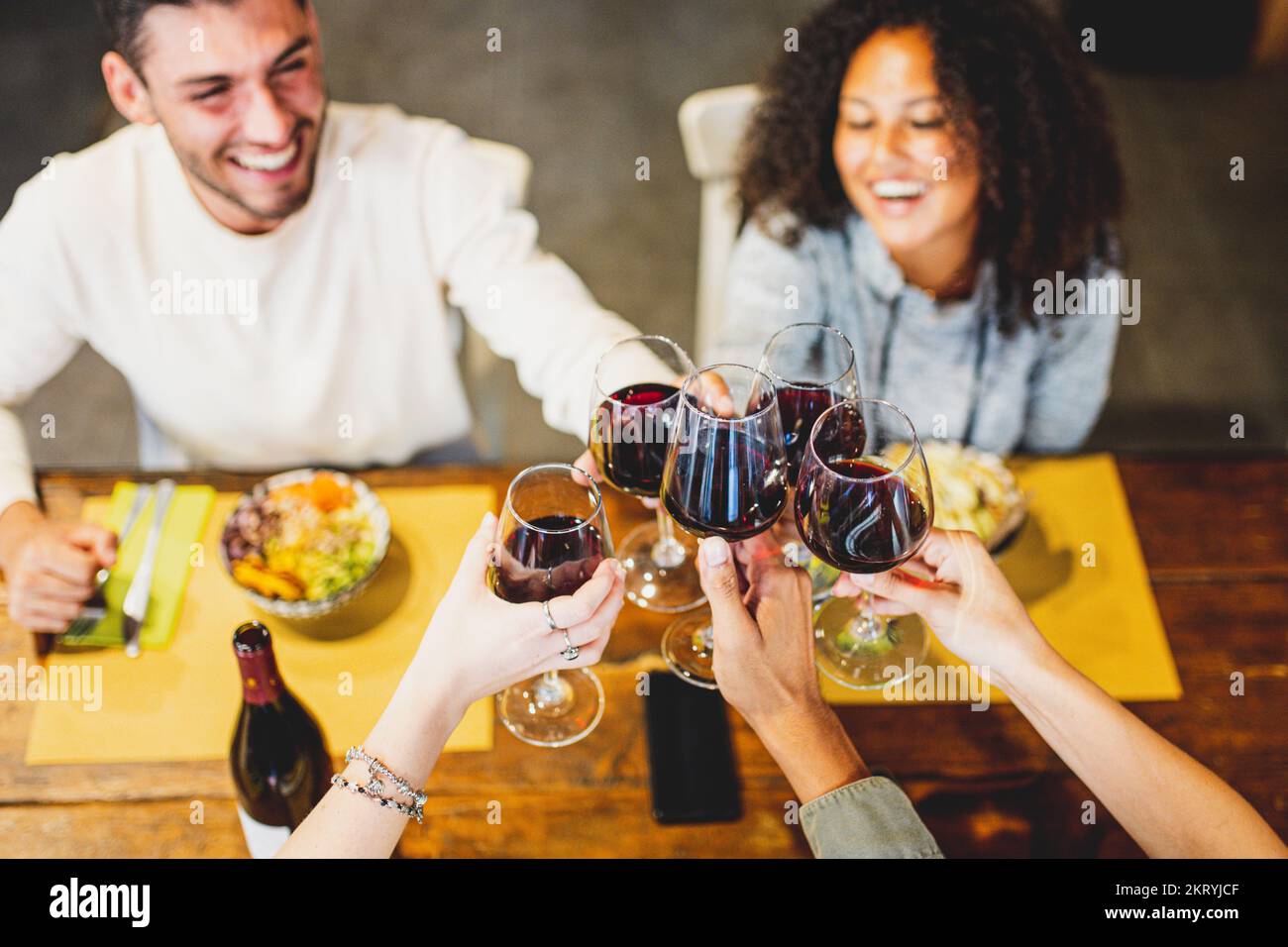 Hands toasting red wine glass and friends having fun cheering at ...