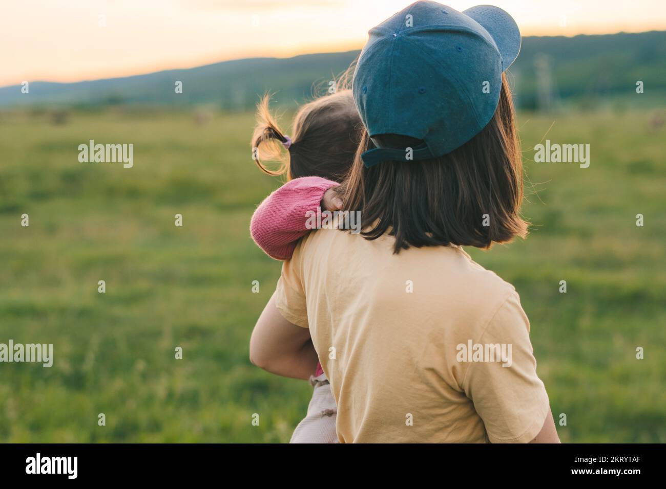 Rear view of a woman holding her baby girl looking at a wide green ...