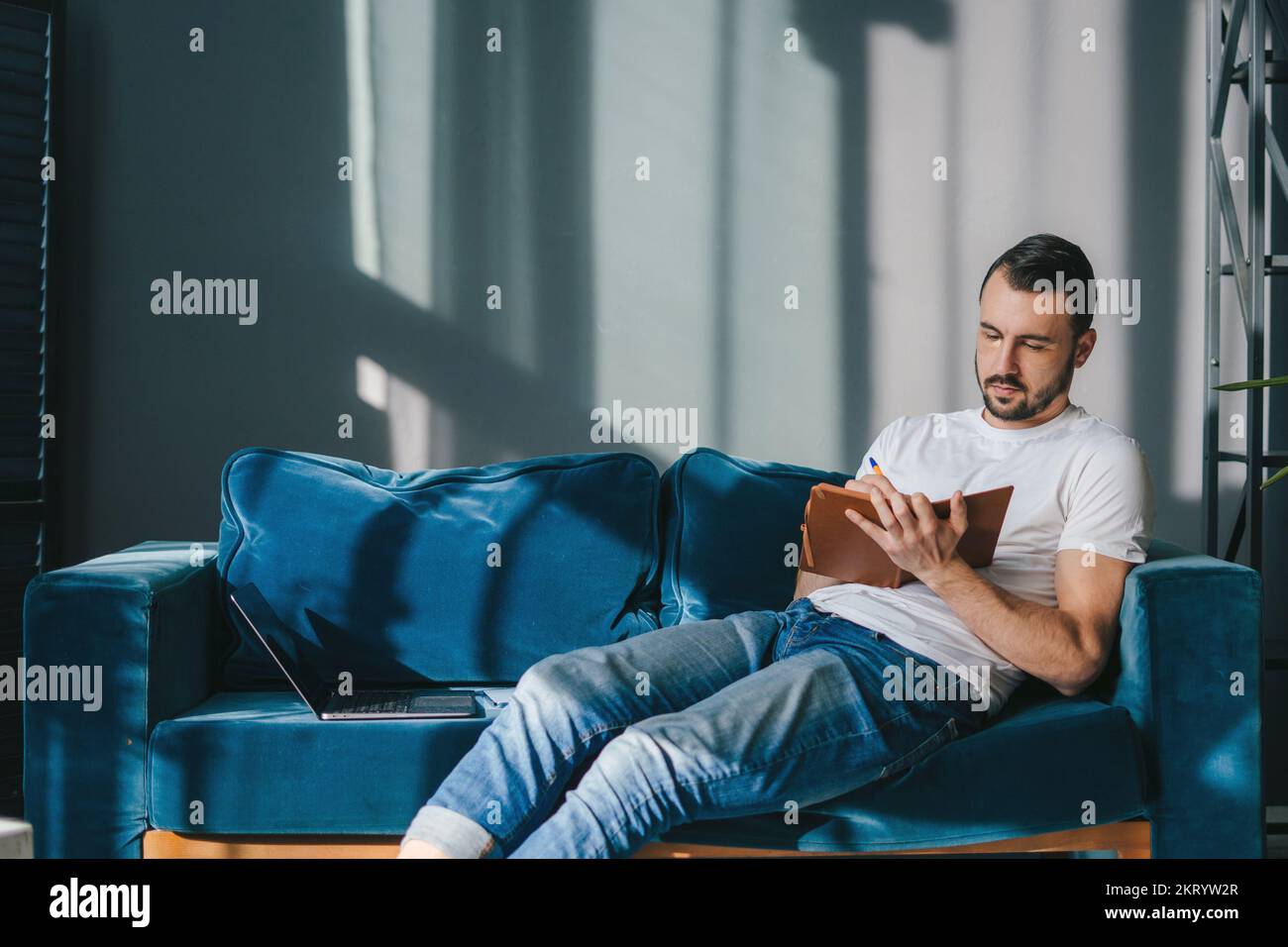 Concentrated young man with pen in hand making notes in notepad sitting ...