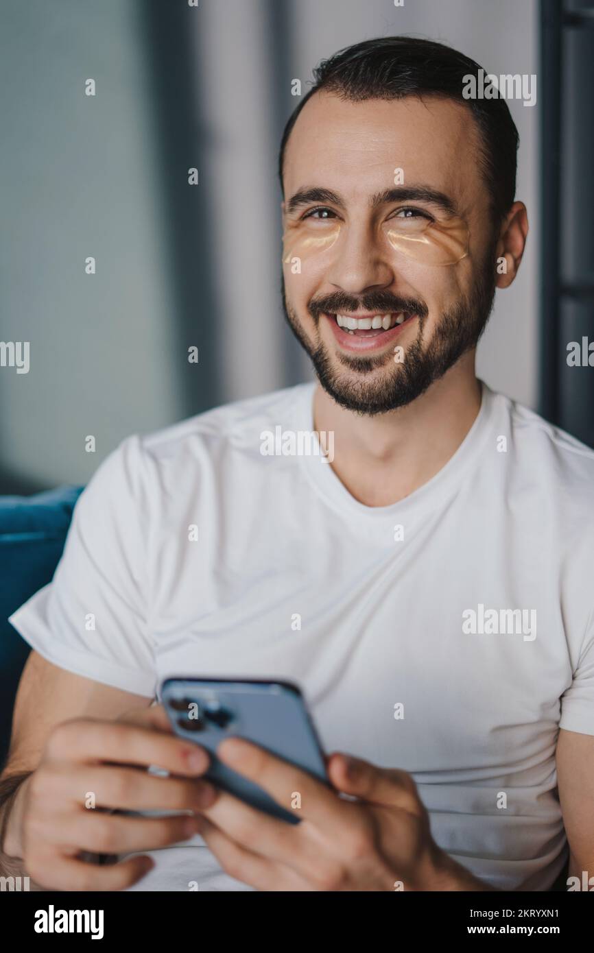 Happy smiling man texting on smartphone at home, while taking care of ...