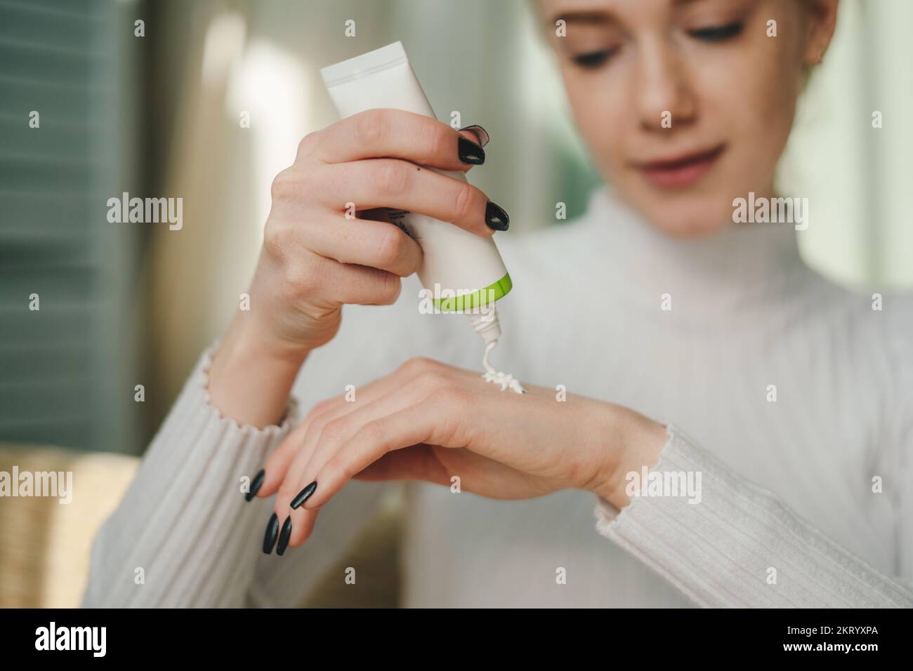 Young woman at home, putting moisturizer white cream on her hands. Skin ...