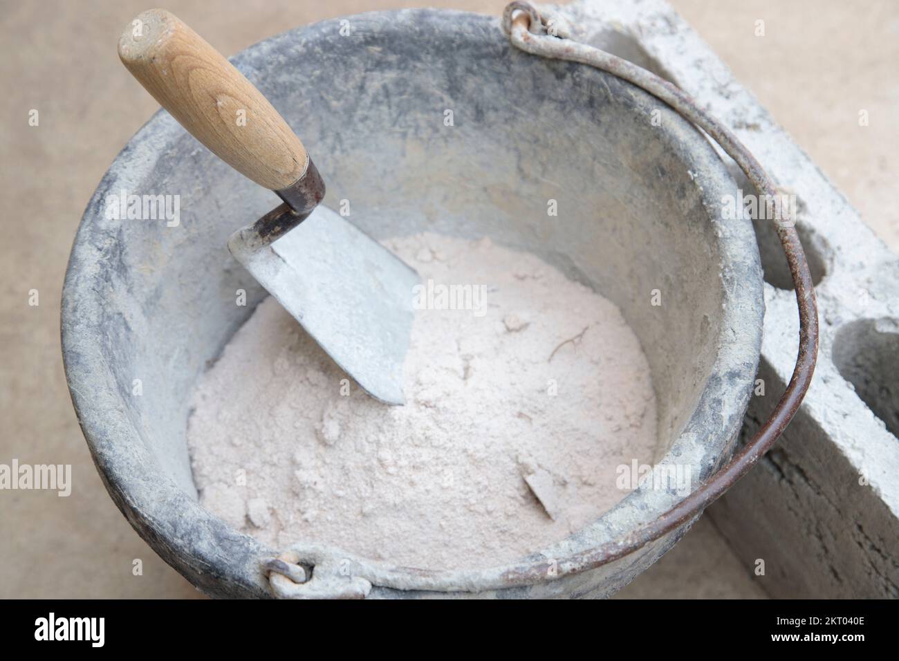 trowel with a wooden handle in a bucket of sand near a four inch ...