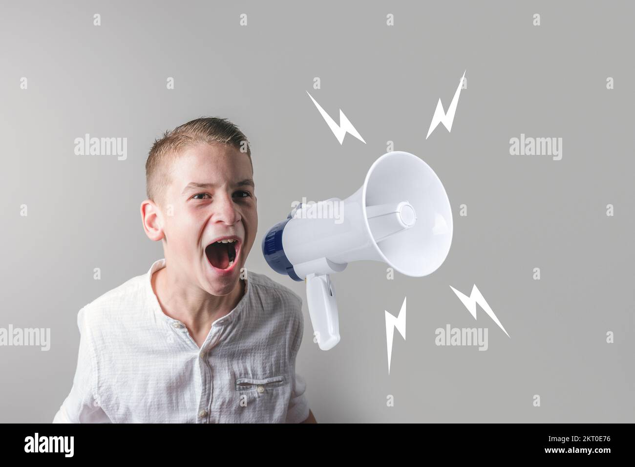 Cute teenager boy in a white shirt using megaphone shouting on gray ...