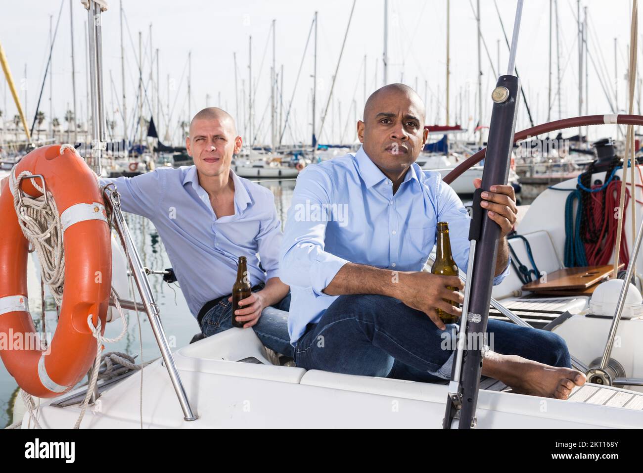 Two men in blue shirts relaxing on sailing yacht in the port Stock ...