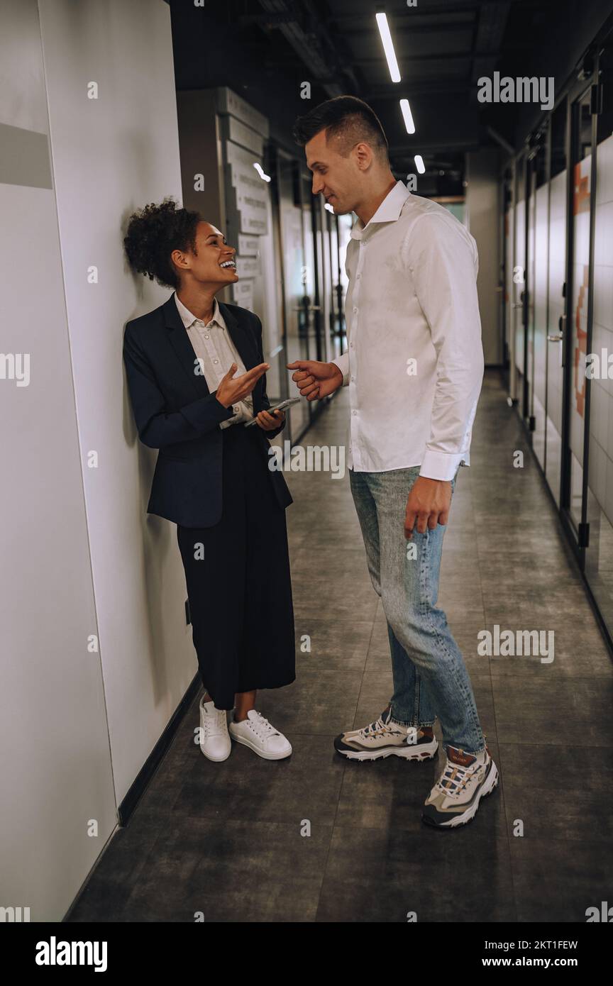 Man and woman standing talking in office corridor Stock Photo - Alamy