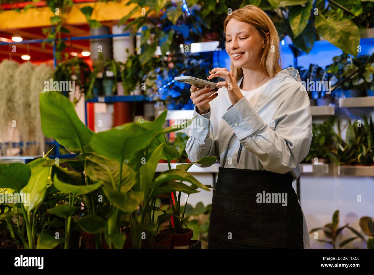 White beautiful young florist girl taking photo of potted plants on ...