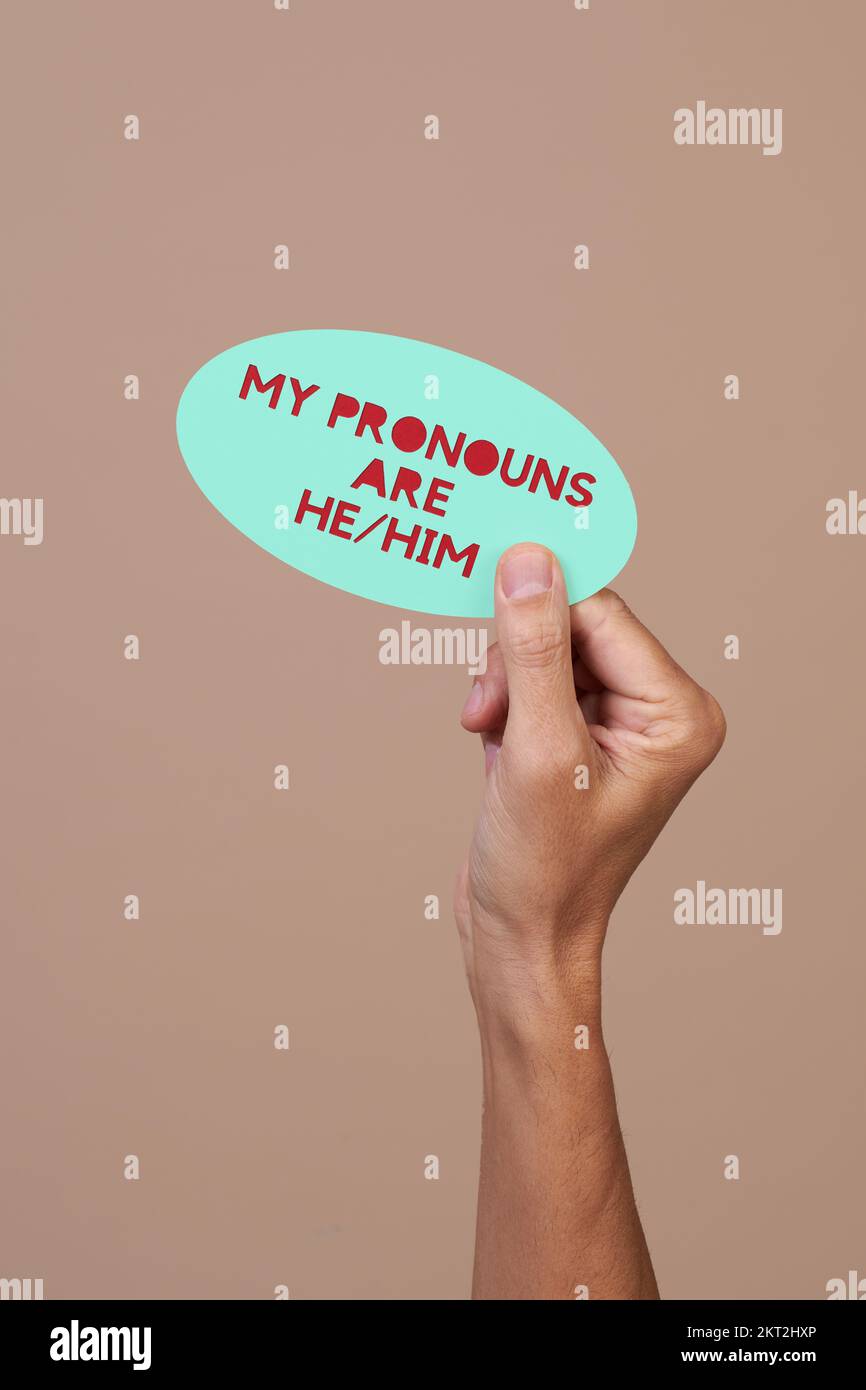 a person holds a green sign with the text my pronouns are he, him ...