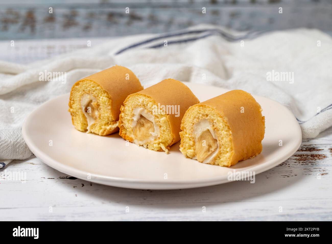 Banana roll cake. Snack roll cake on a white wood background. close up ...