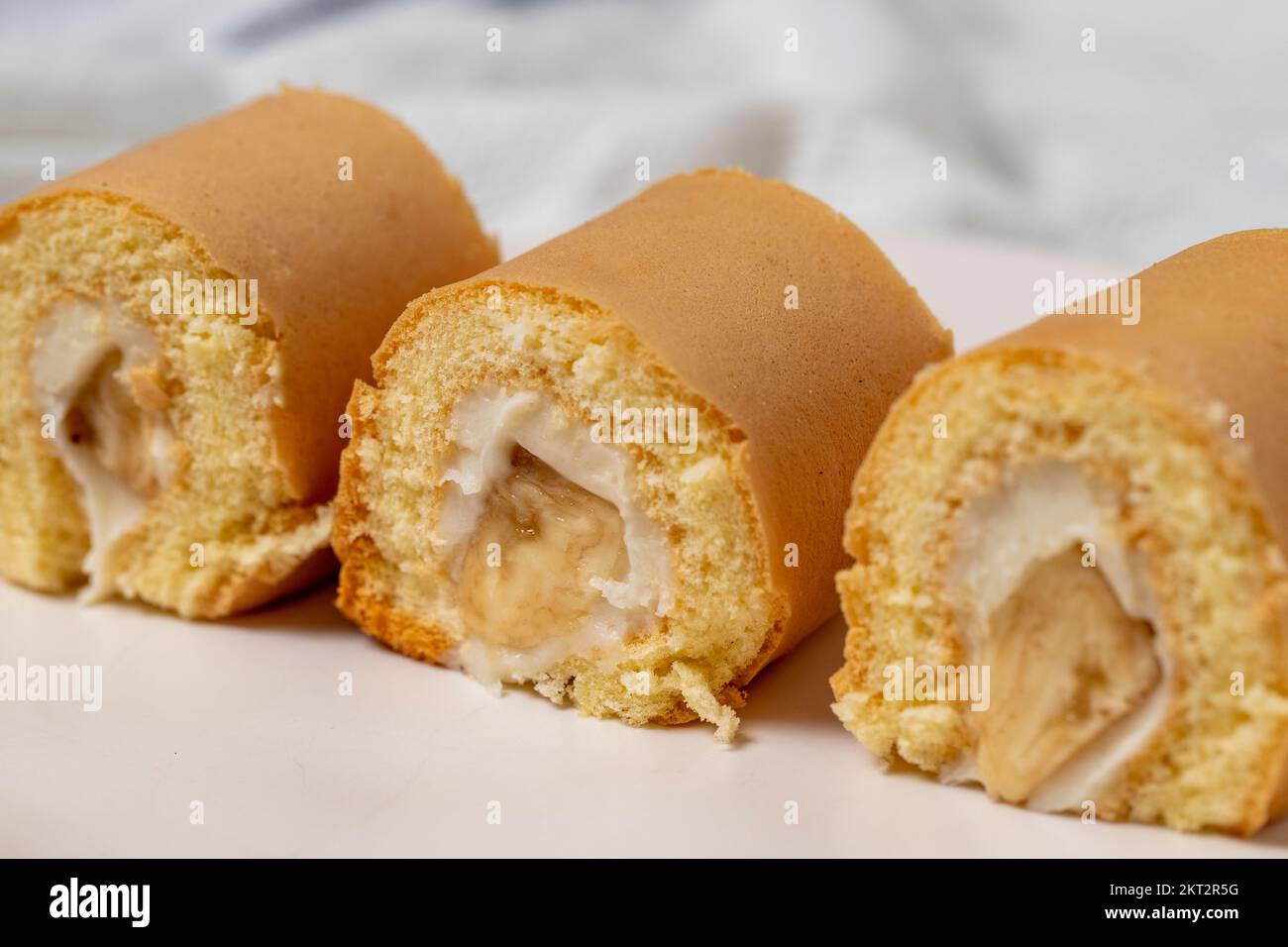 Banana roll cake. Snack roll cake on a white wood background. close up ...