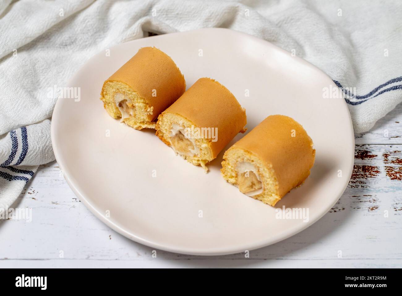 Banana roll cake. Snack roll cake on a white wood background. close up ...