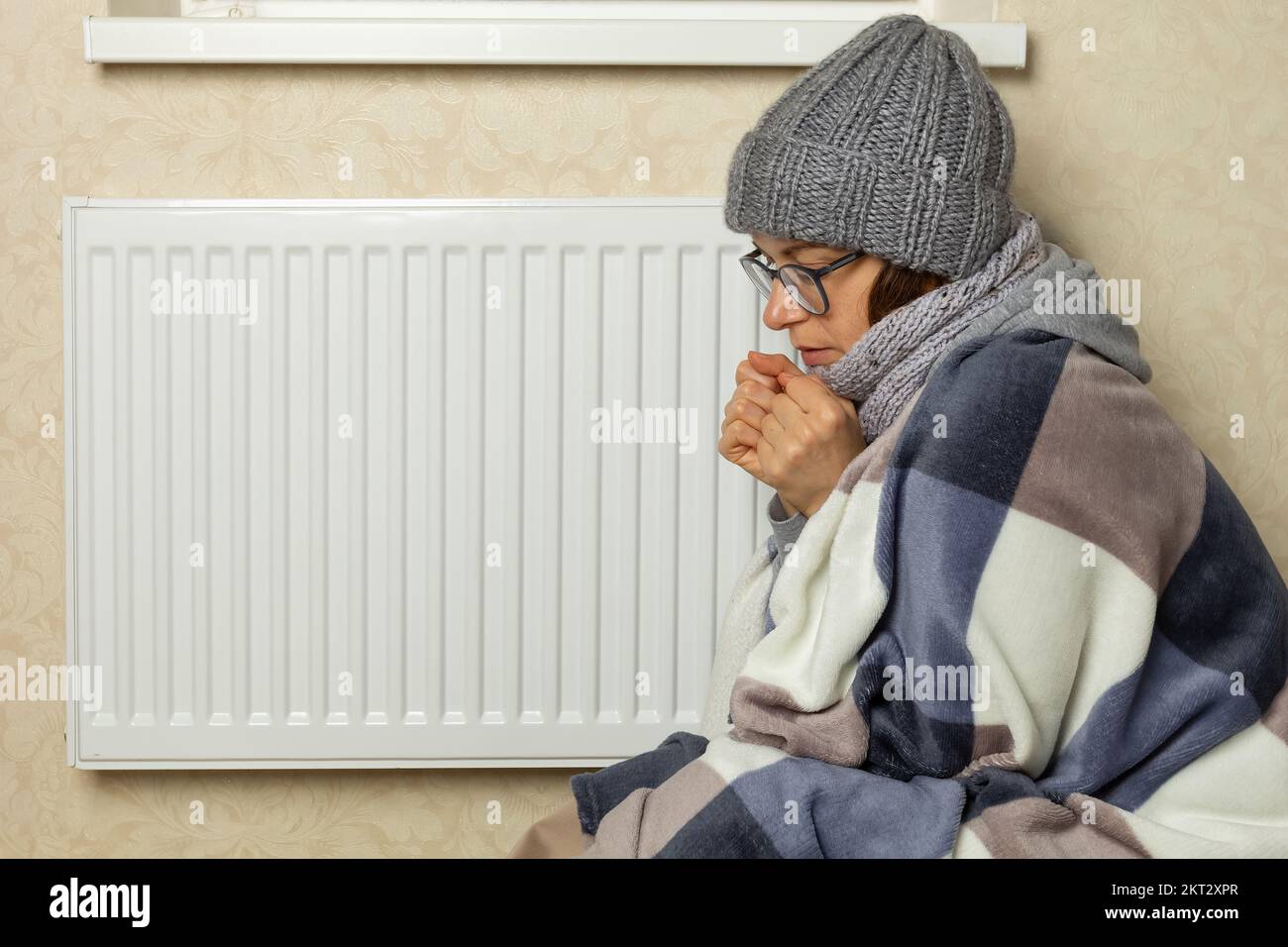 A woman in a cold room, wrapped in a blanket, warms herself near the ...