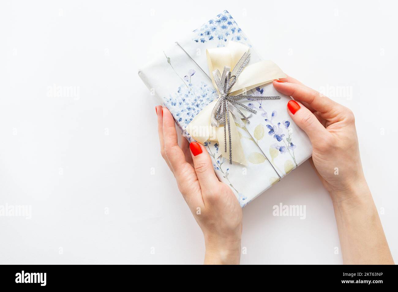 The girl holds a beautifully wrapped gift in her hands on a white ...