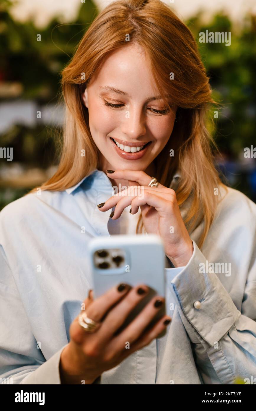 White beautiful young florist girl smiling and using cellphone while ...
